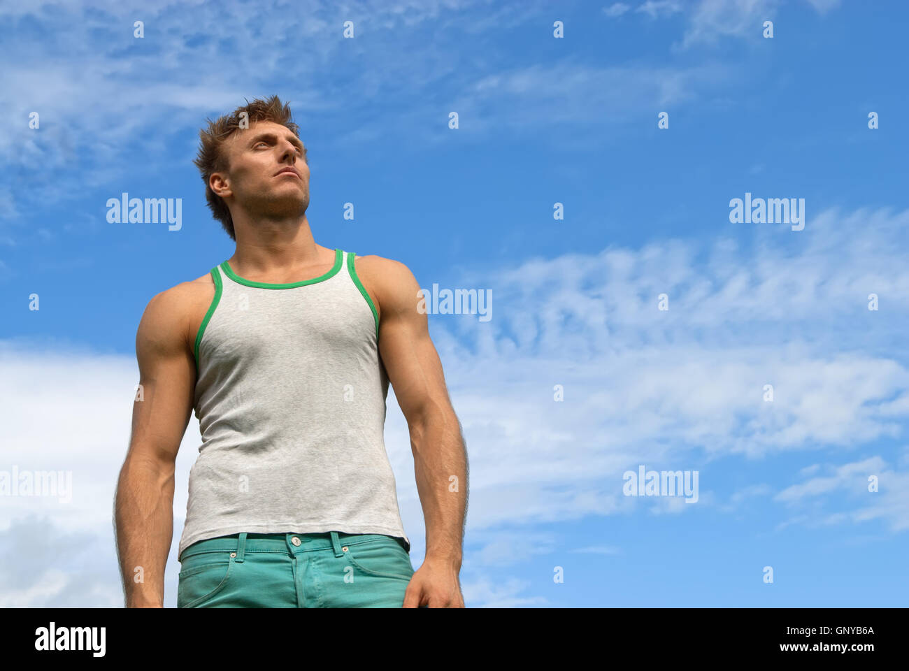 Strong young man on blue sky background Stock Photo - Alamy