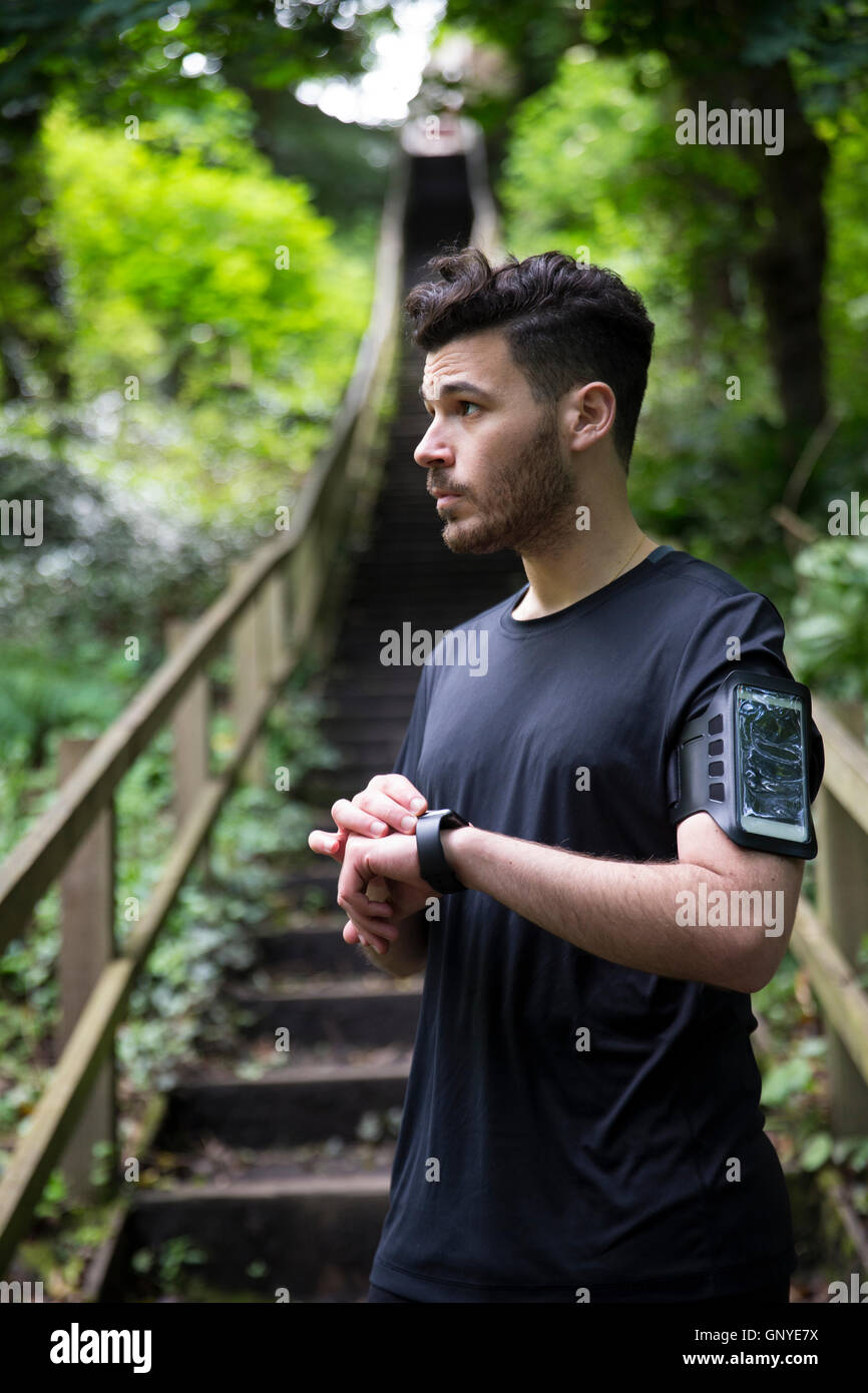 Man out running on forest trail, using his smart watch heart rate ...