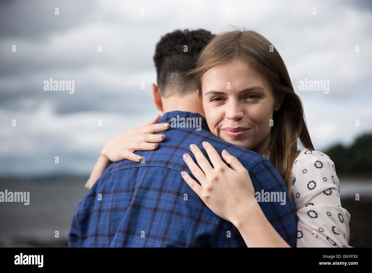 Relaxed young couple hugging while walking along pebble beach ...