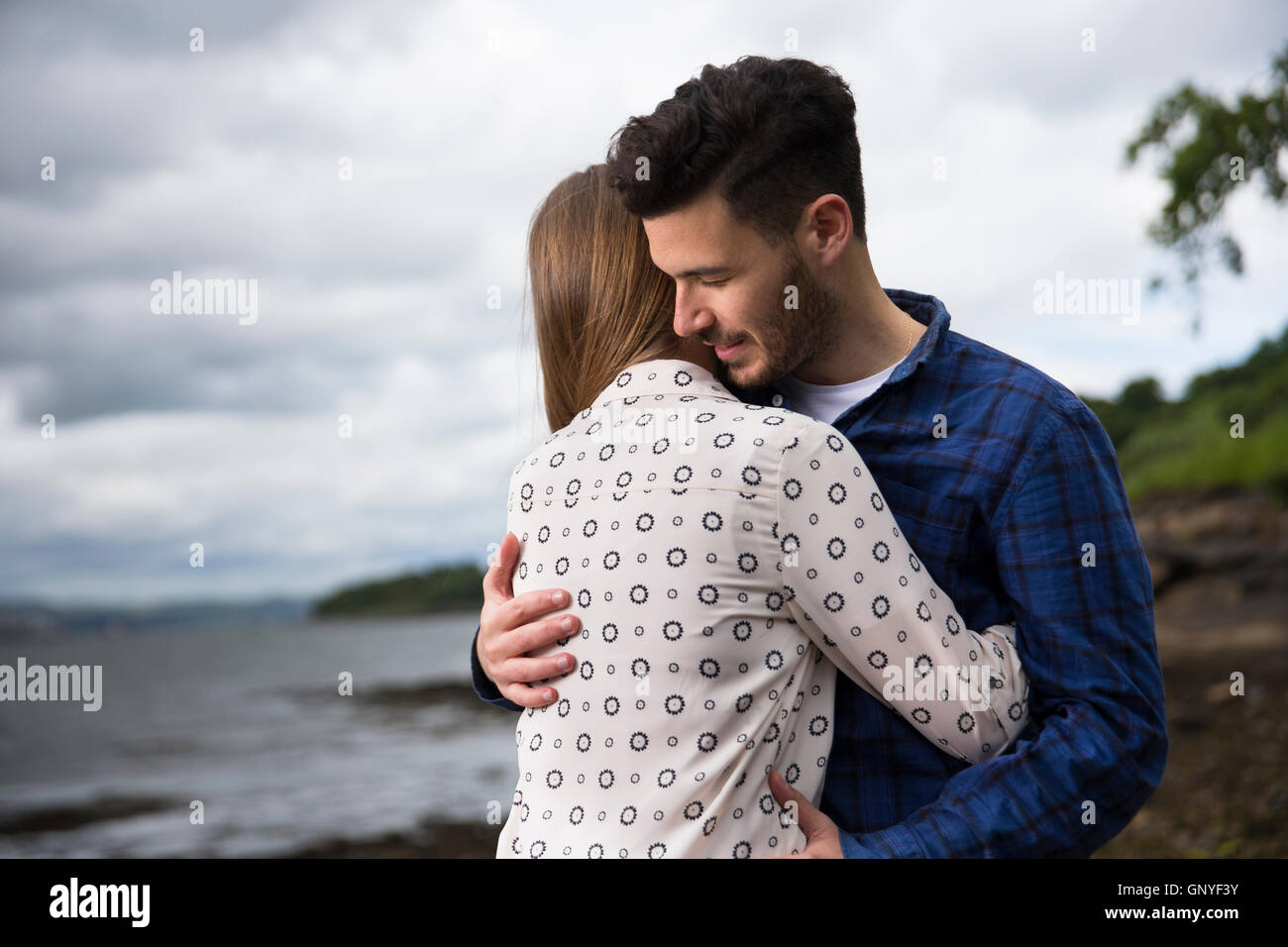 Relaxed Young Couple Hugging While Walking Along Pebble Beach