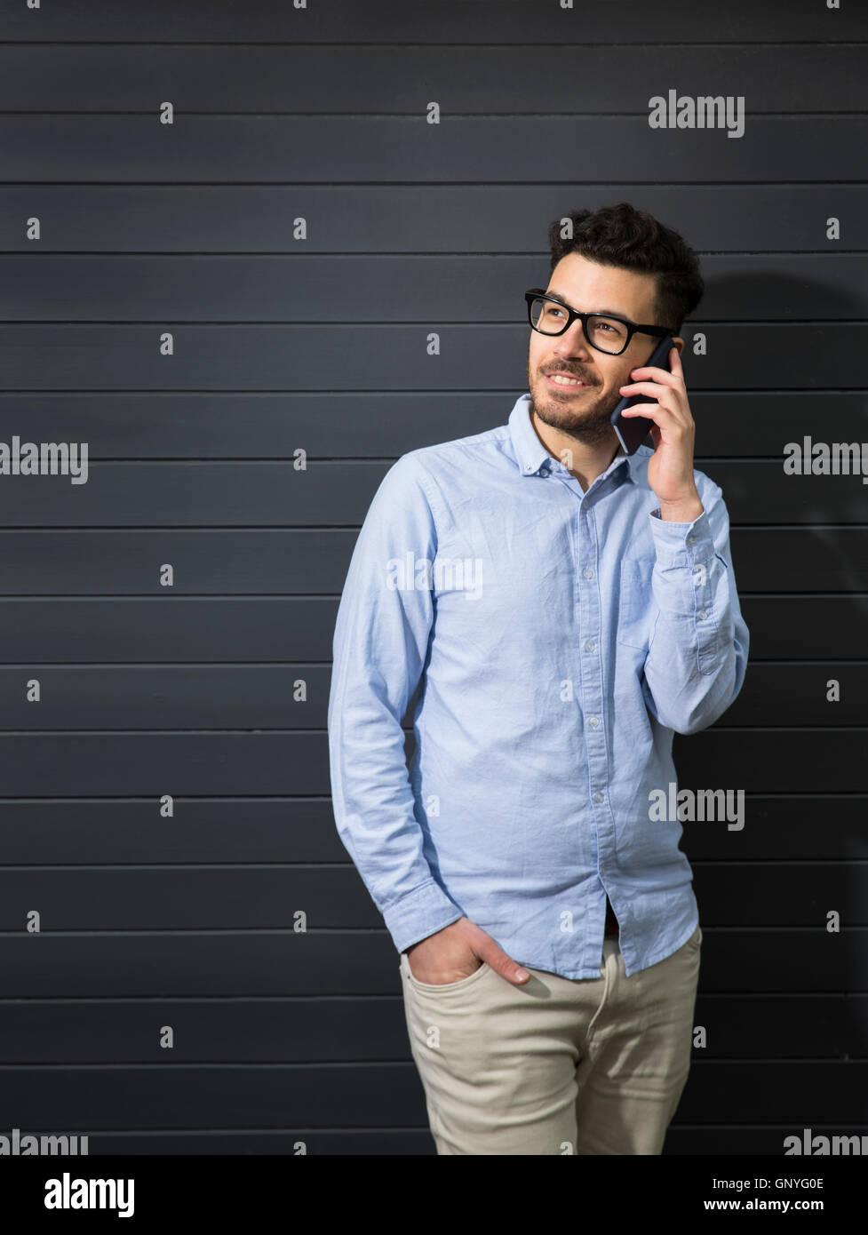 Happy Man standing using his smart phone and leaning on a dark grey ...