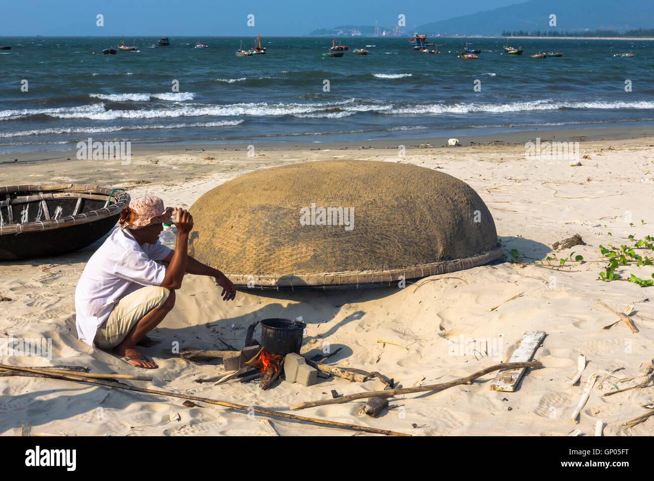 Da Nang Bay: fisherman tends his fire on the beach, with local coracles ...