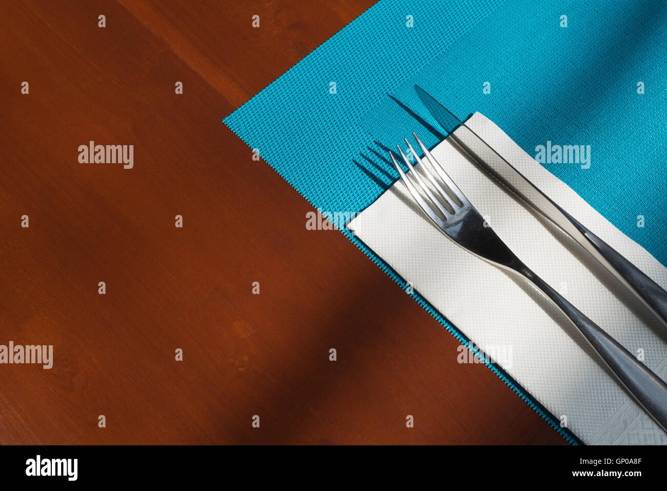 Silverware and tissue and blue mat napery on brown wooden table. Simple ...