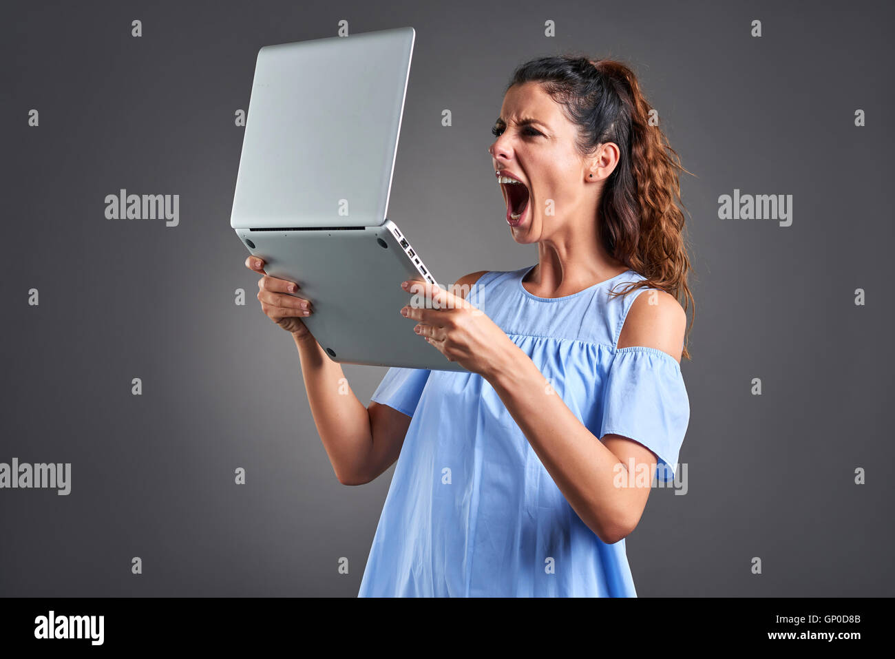 A beautiful young woman standing and screaming while grabbing a laptop ...