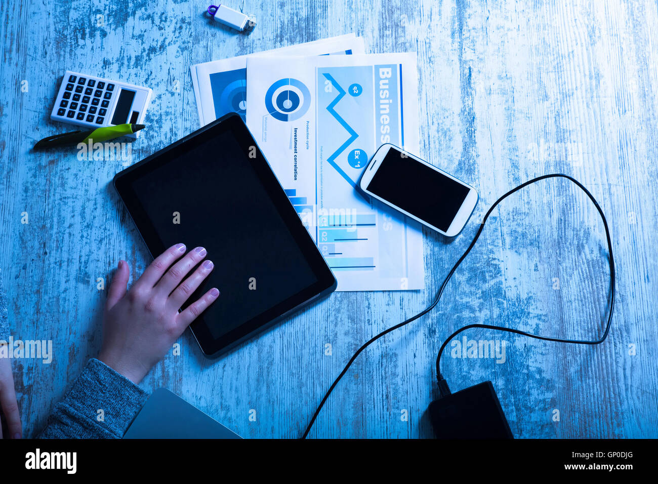 A working woman’s hand at night at a table with laptop, tablet and ...