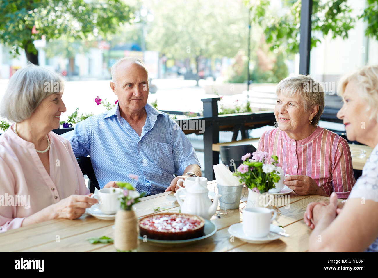 Friendly elderly people gathered by table in outdoor cafe Stock Photo ...