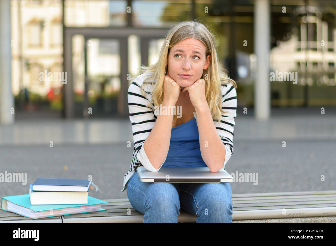 Doubtful female blond teenager with furrowed eyebrows leaning on knees ...
