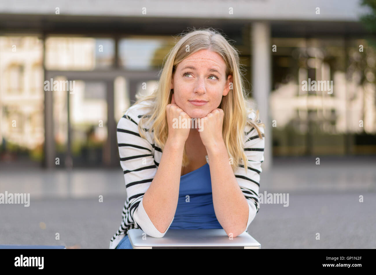 Doubtful female blond teenager with furrowed eyebrows leaning on knees ...