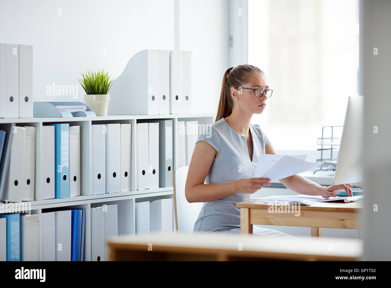 Young female office worker at computer desk sorting documentation and ...
