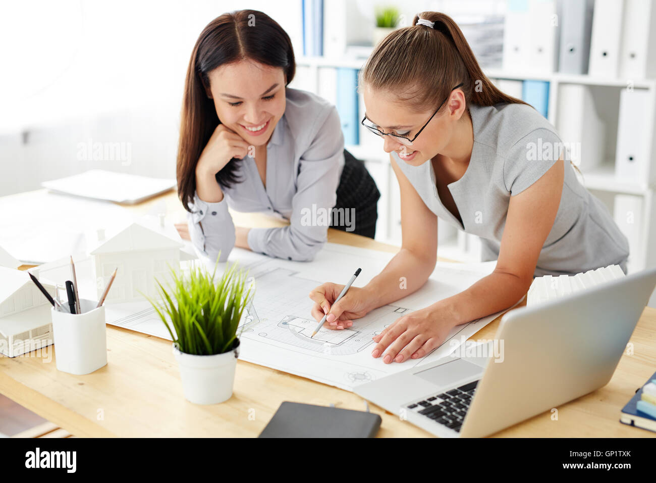 Two young female office workers standing at desk bending over schemes ...