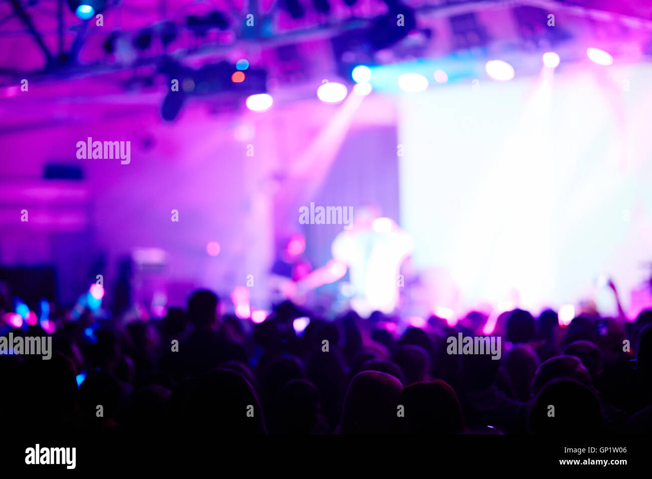Blurred image of performer on purple-lit stage before large crowd of ...
