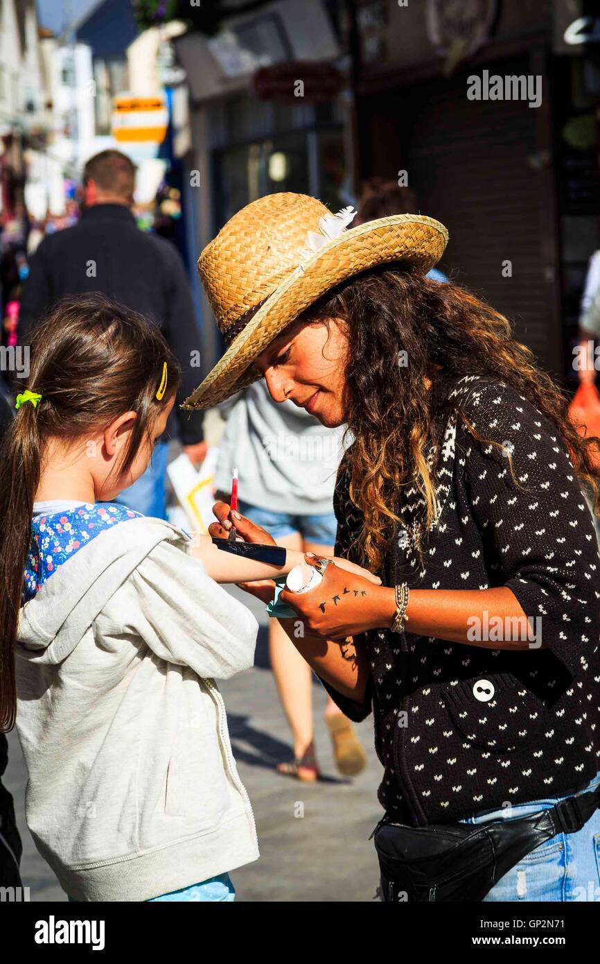 A lady street artist putting a senna tattoo on a young girl's arm in ...