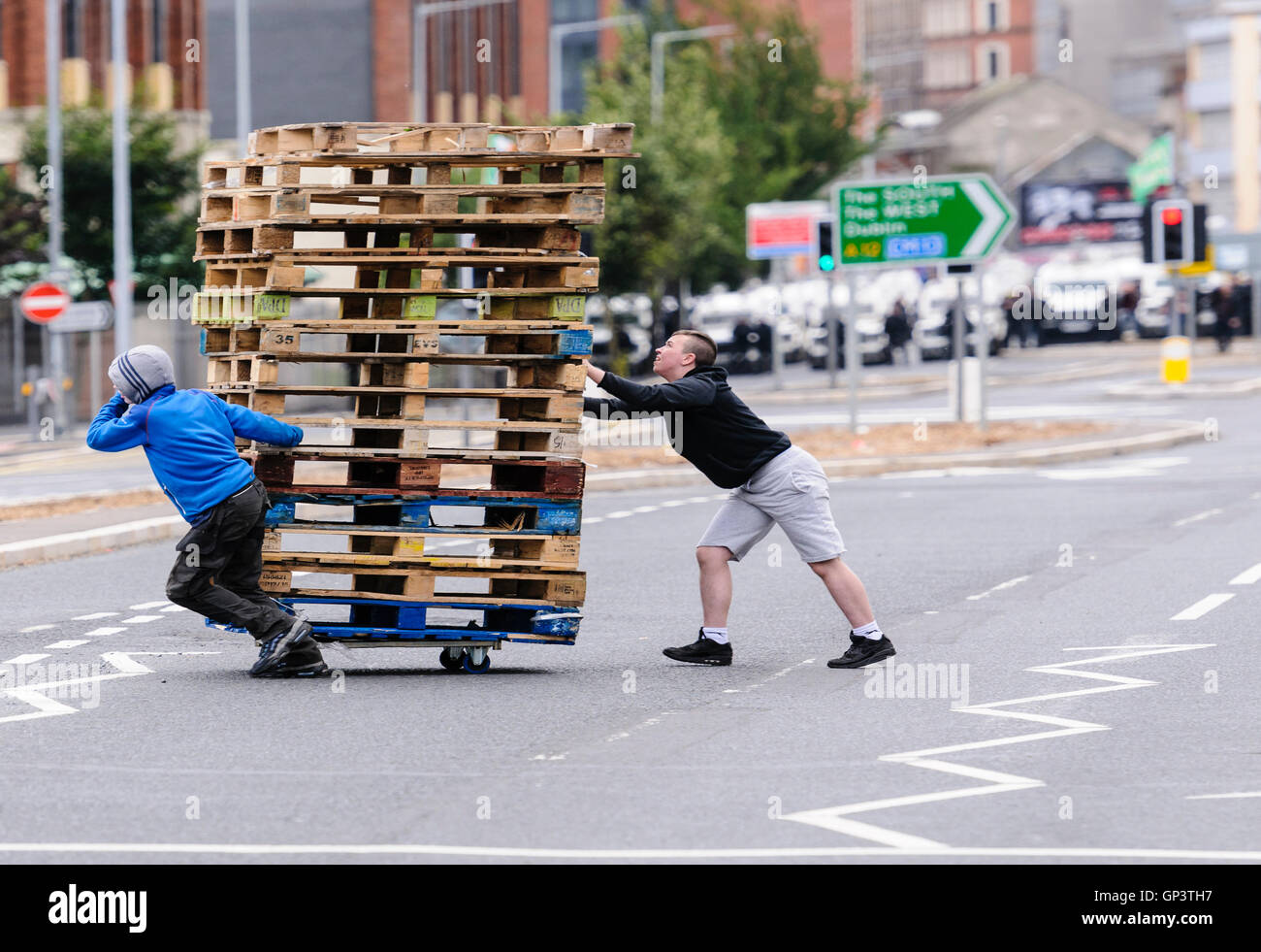Two boys push a stack of wooden pallets for a bonfire across a road in ...