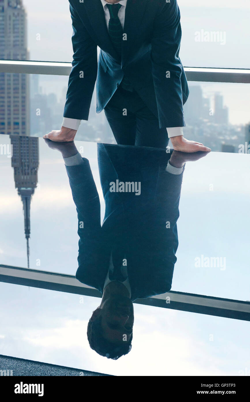 Businessman leaning against table, reflection in glass top Stock Photo ...