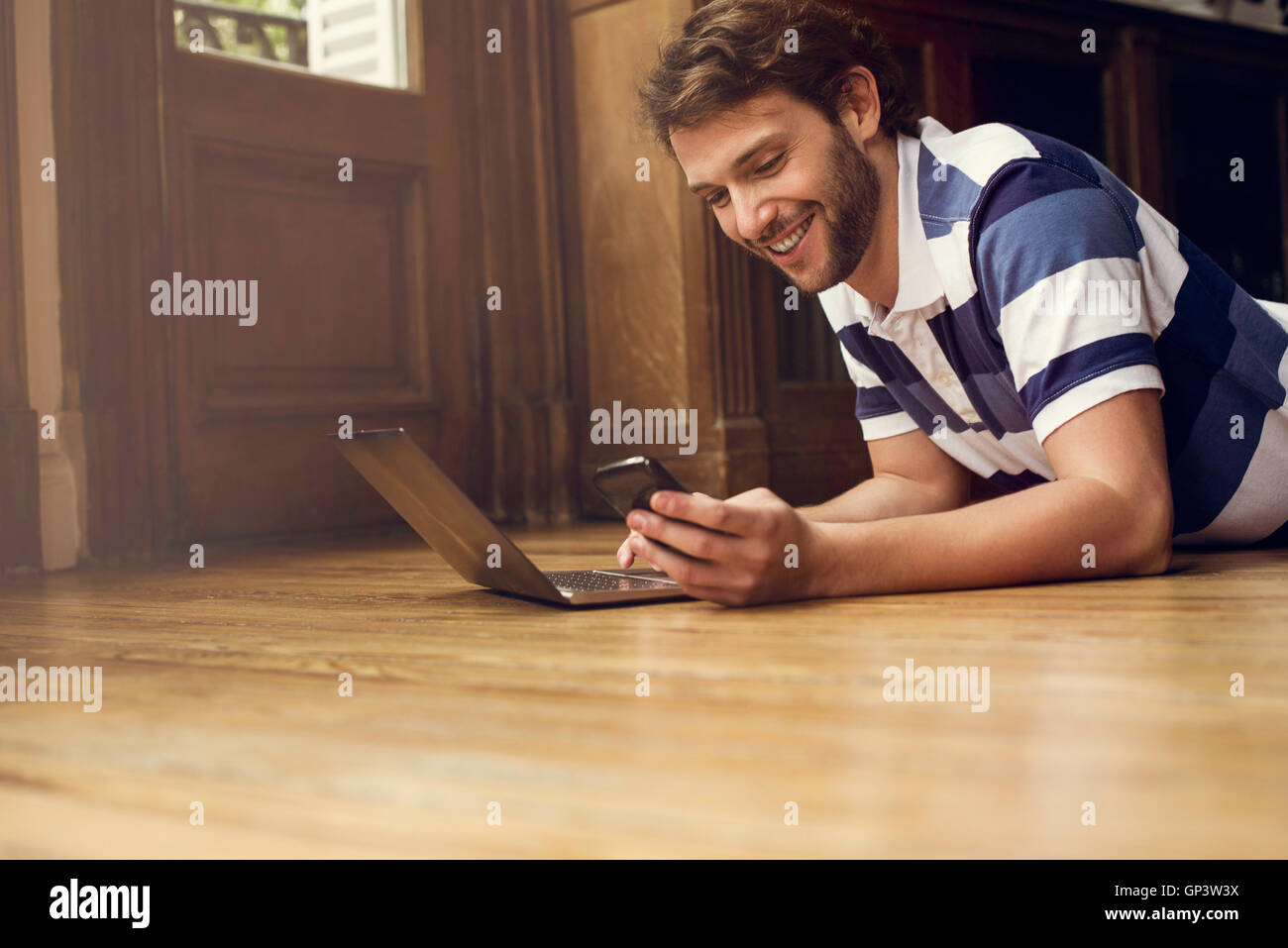 Man lying on floor using laptop and smartphone Stock Photo - Alamy