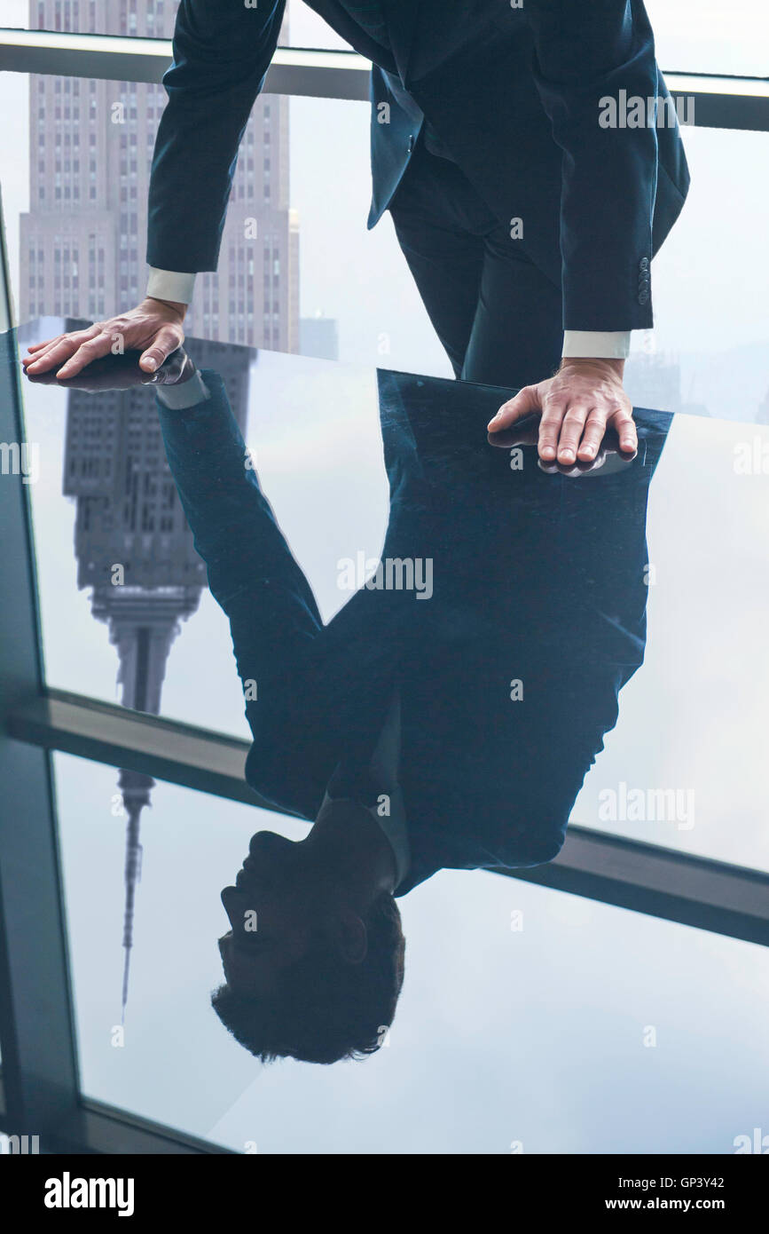 Businessman leaning against table, reflection in glass top Stock Photo ...