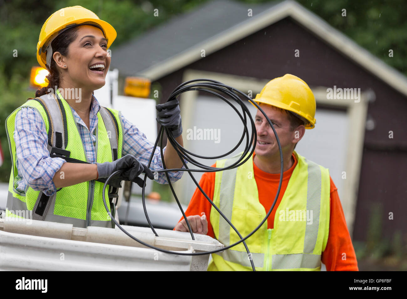 Happy Hispanic female cable lineman stringing a new line in the rain ...