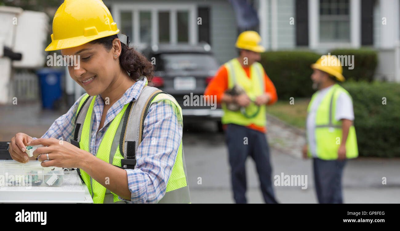 Hispanic female utility worker with box of cable amplifiers at site ...