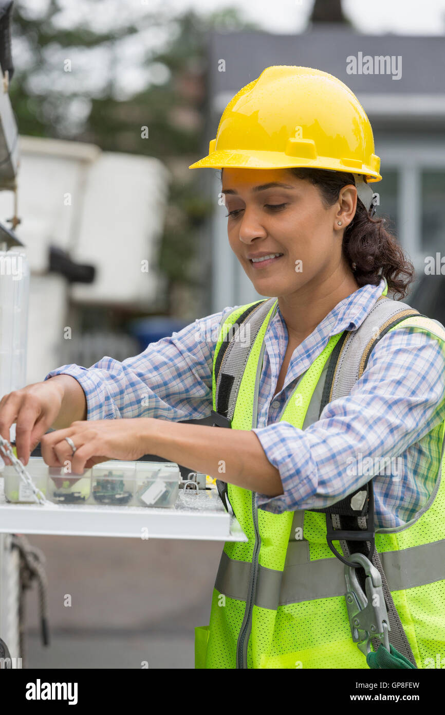 Hispanic female utility worker with box of cable amplifiers at site ...