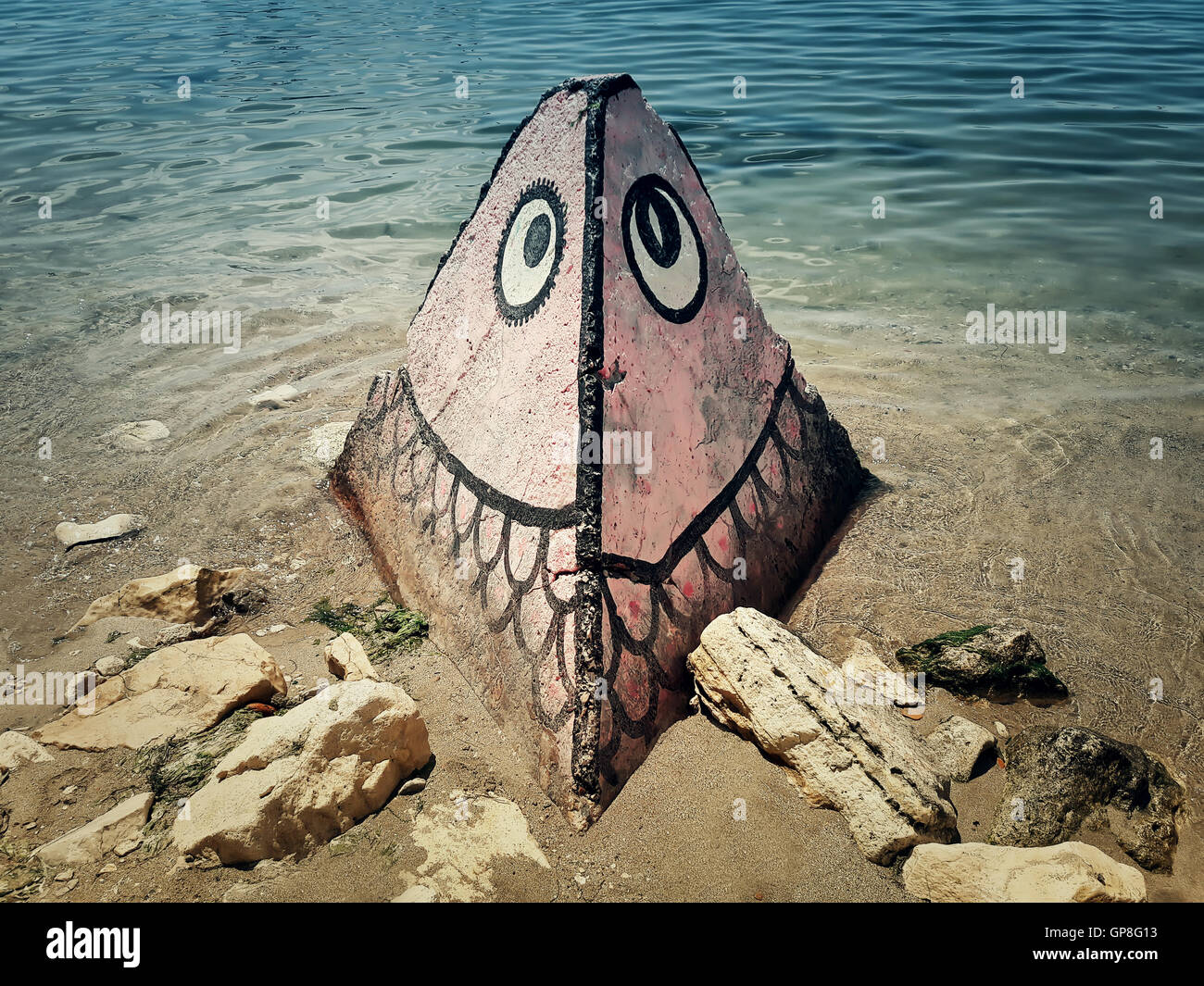 A big stone with graffiti standing on the beach shore near the water ...