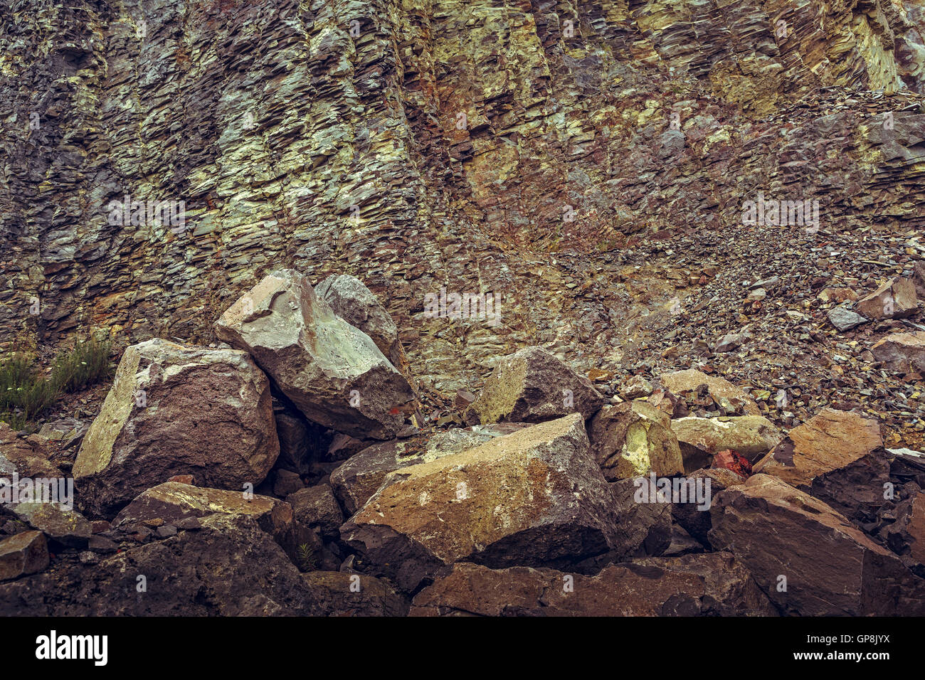 Vertical strata rock wall and big boulders in an deserted basalt quarry ...