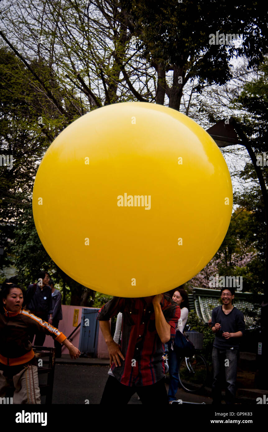 A street performer performs with a large yellow balloon in Ueno Park ...