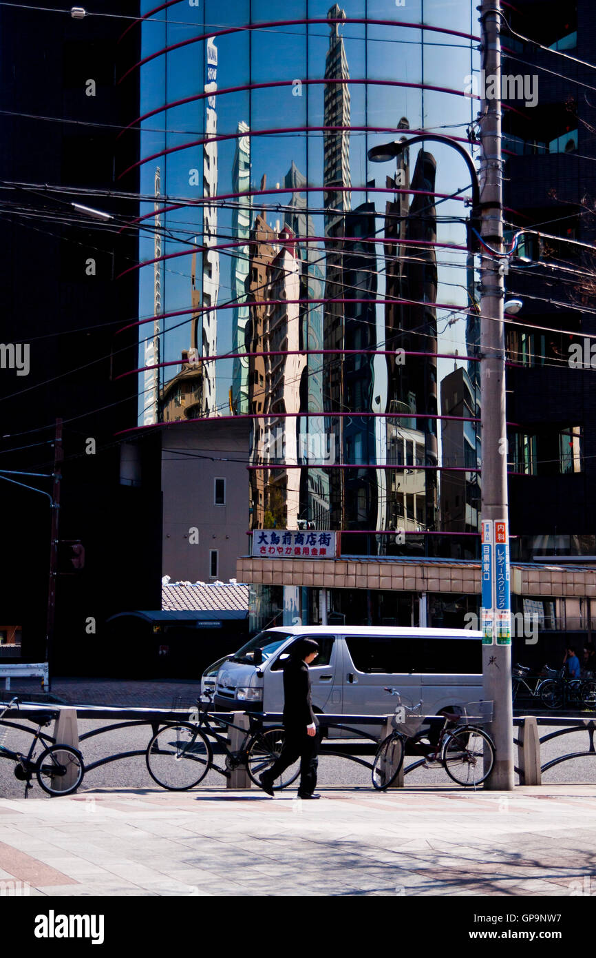 A pedestrian walks past buildings reflected in an office block facade ...