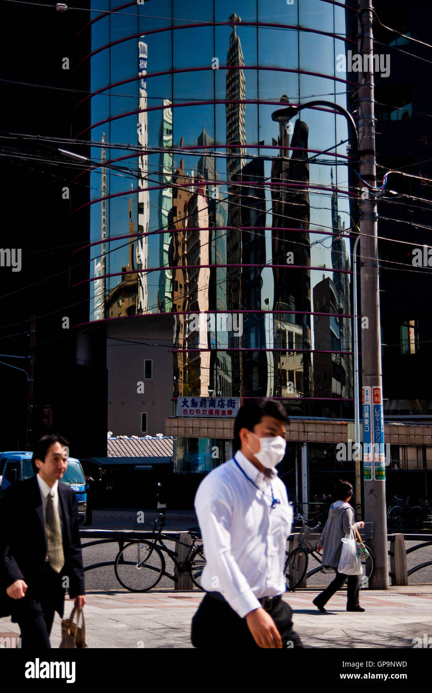 Pedestrians walk past buildings reflected in an office block facade in ...