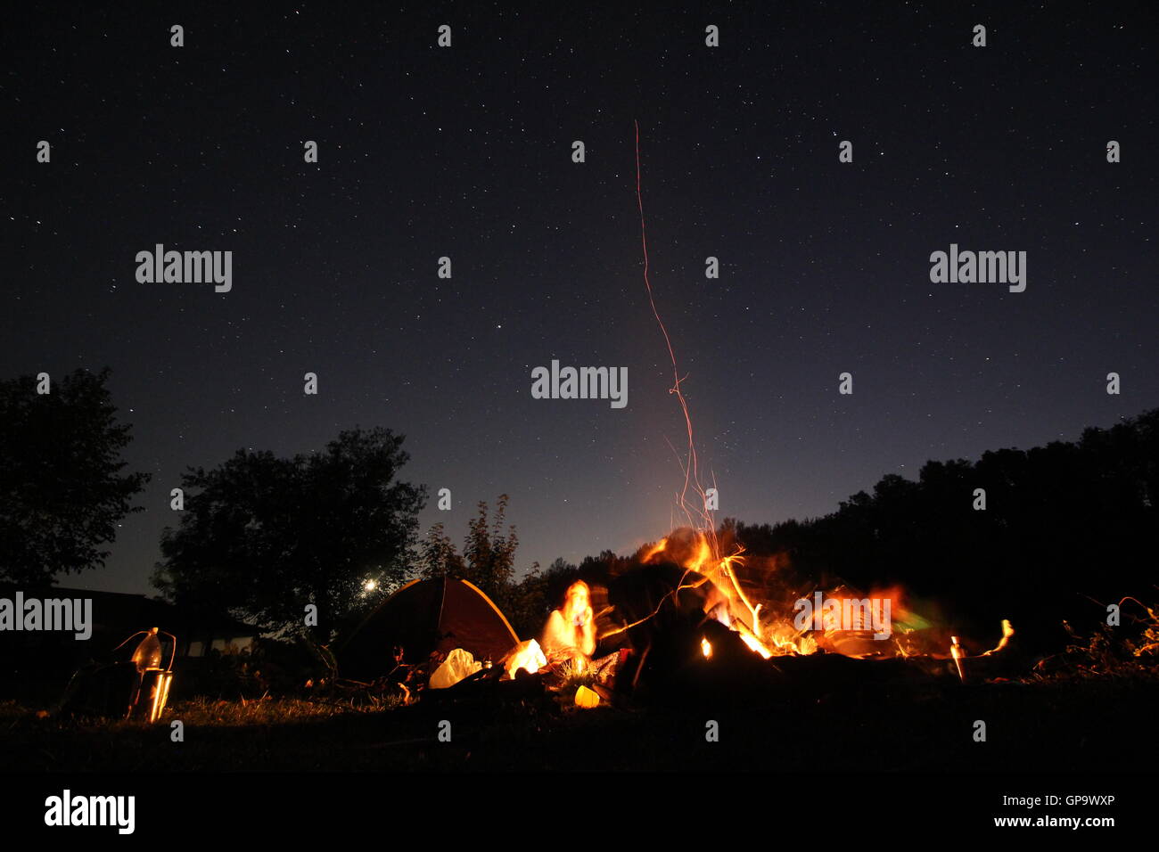 Night time campfire scene with people sat round campfire with stars in ...