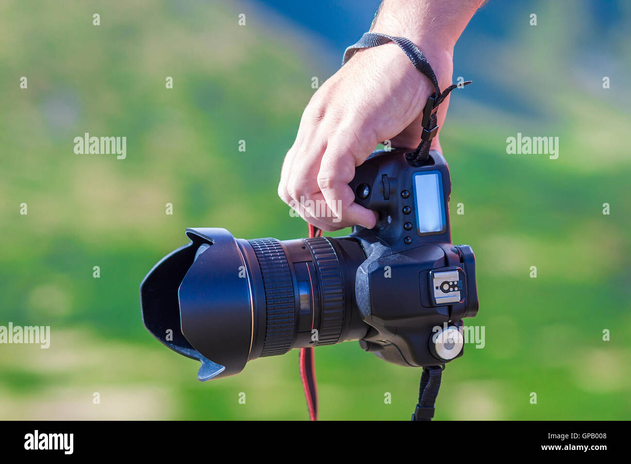 Hand of a man holding professional digital camera on blurred green ...