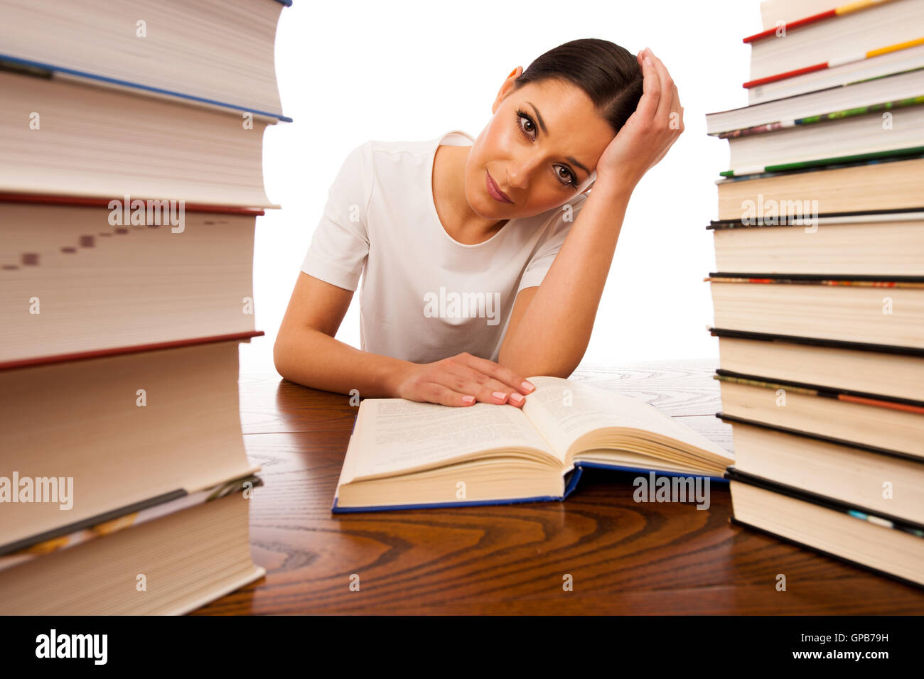 Sick and tired woman reading behind the table between two pile of books ...