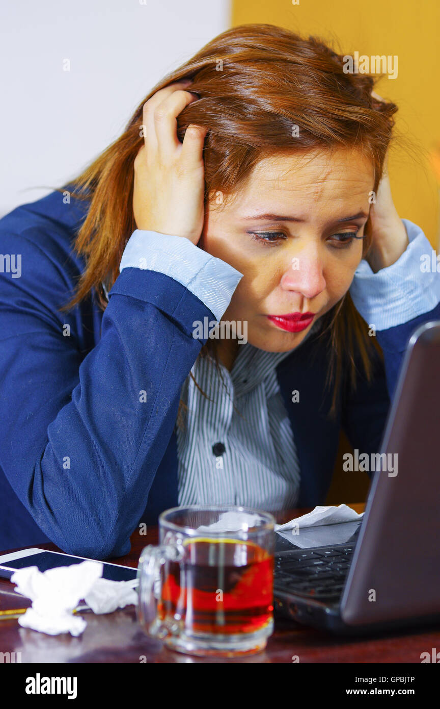 Young woman sick with flu, sitting by table using computer working ...