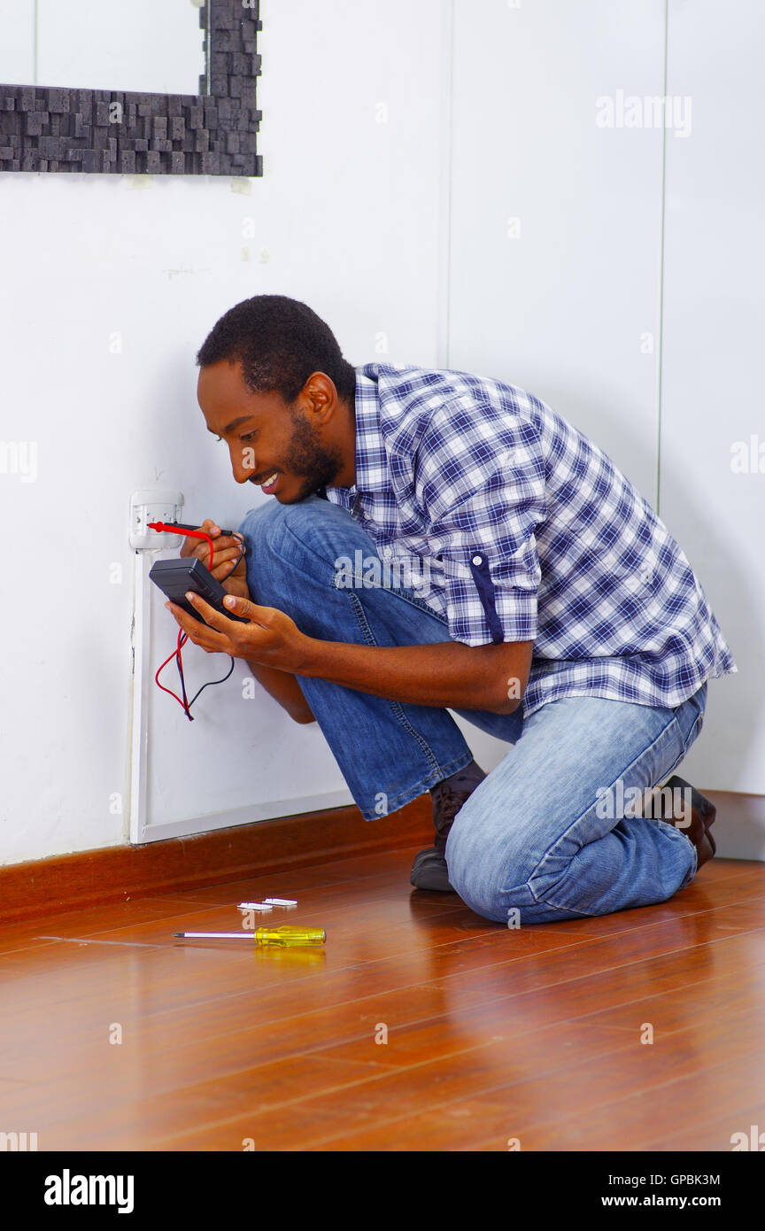 Man wearing white and blue shirt working on electrical wall socket ...