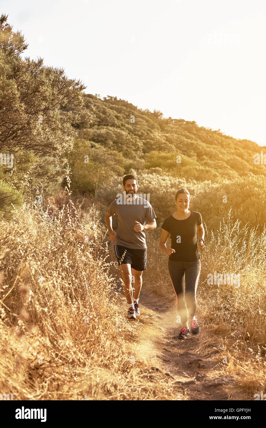 Two people running down a dusty path in full sun light with shrubs ...
