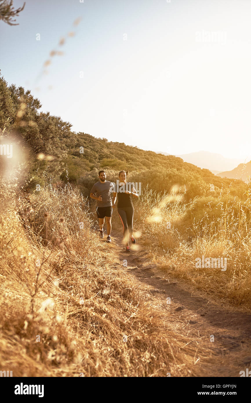 Couple running down a dusty path in full sun light from very far away ...