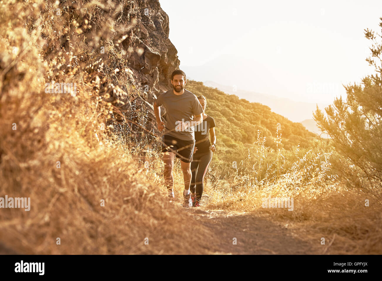 Lovely young couple running down a dusty path in full sun light with ...