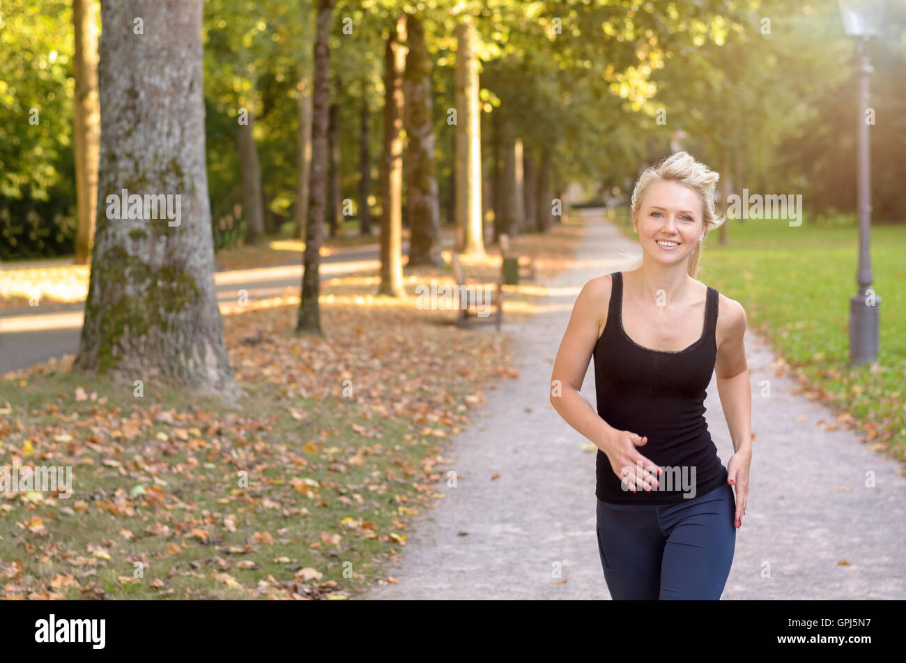Athletic pretty young blond woman jogging in a park approaching the ...
