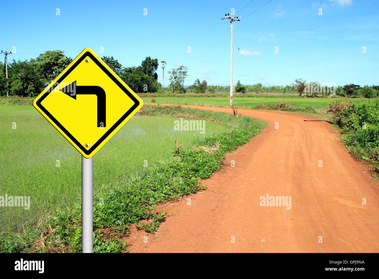 Turn left warning sign with soil road Stock Photo - Alamy