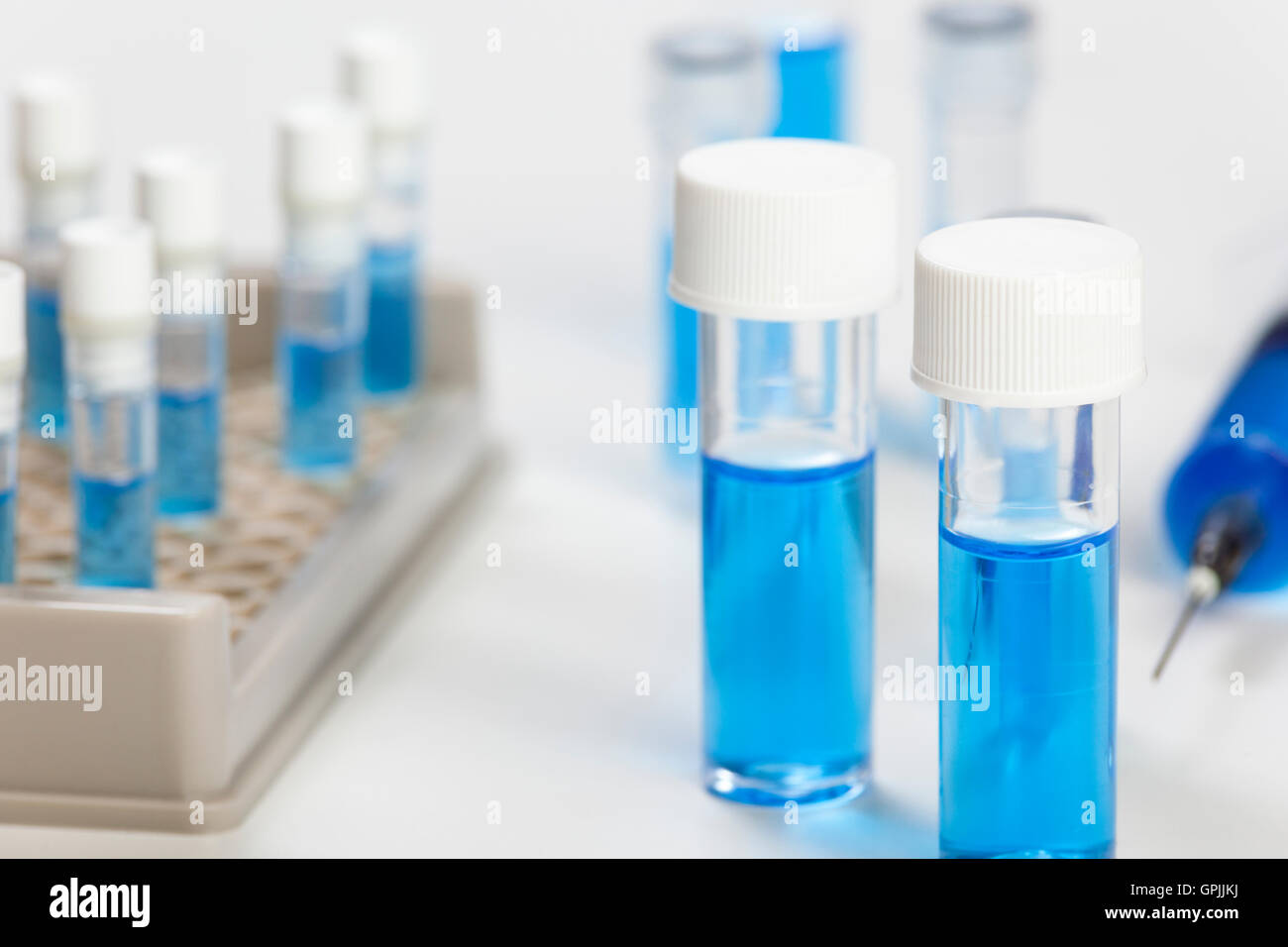 Close up of a vial containing a blue fluid with a syringe on a white ...