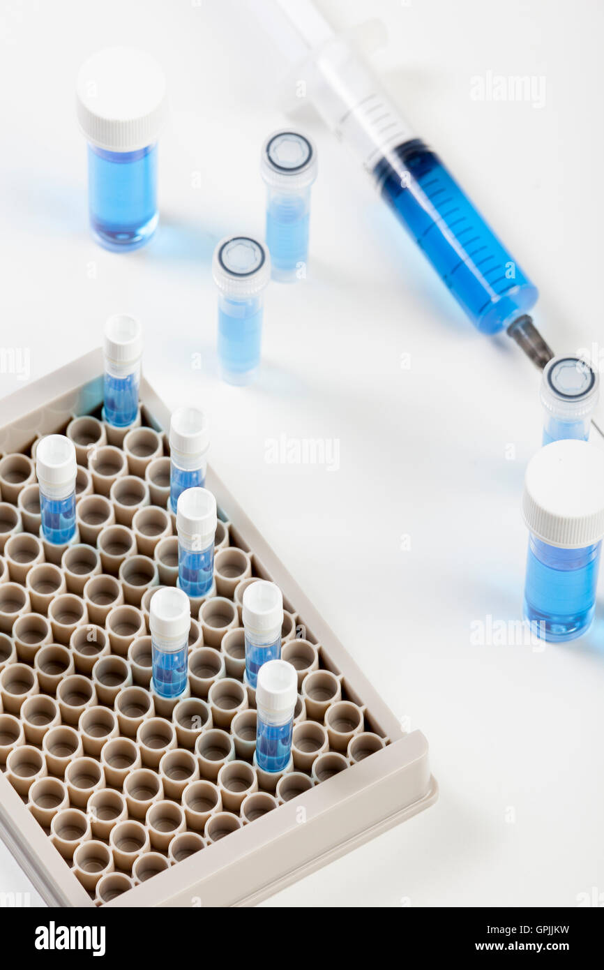 Loaded syringe and capped vials containing a blue fluid on a white ...