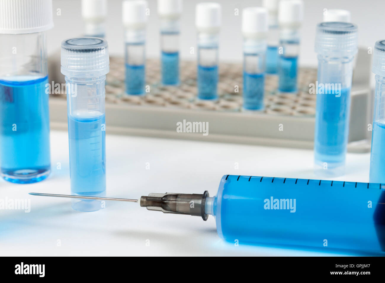 Syringe and capped vials containing blue fluid on white laboratory ...