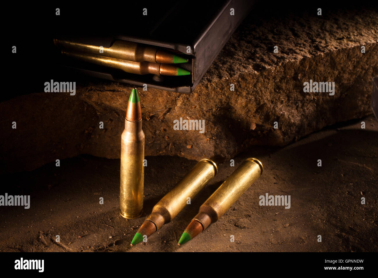 Three cartridges with green tipped bullets and a magazine on rocks ...
