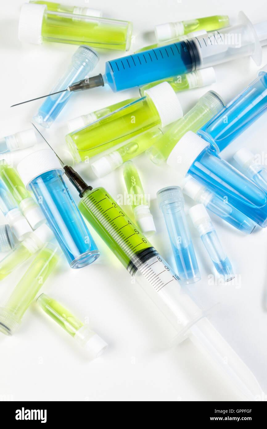 Loaded syringe's and vials containing blue and green fluids on a white ...