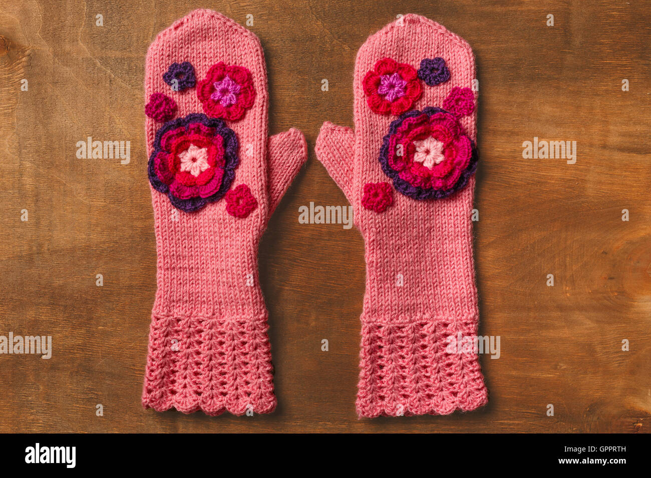 Pink knitted mittens with flowers on wooden background Stock Photo - Alamy