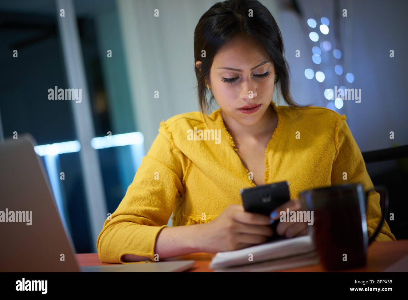 Young woman using smartphone while doing homework at night. Female ...