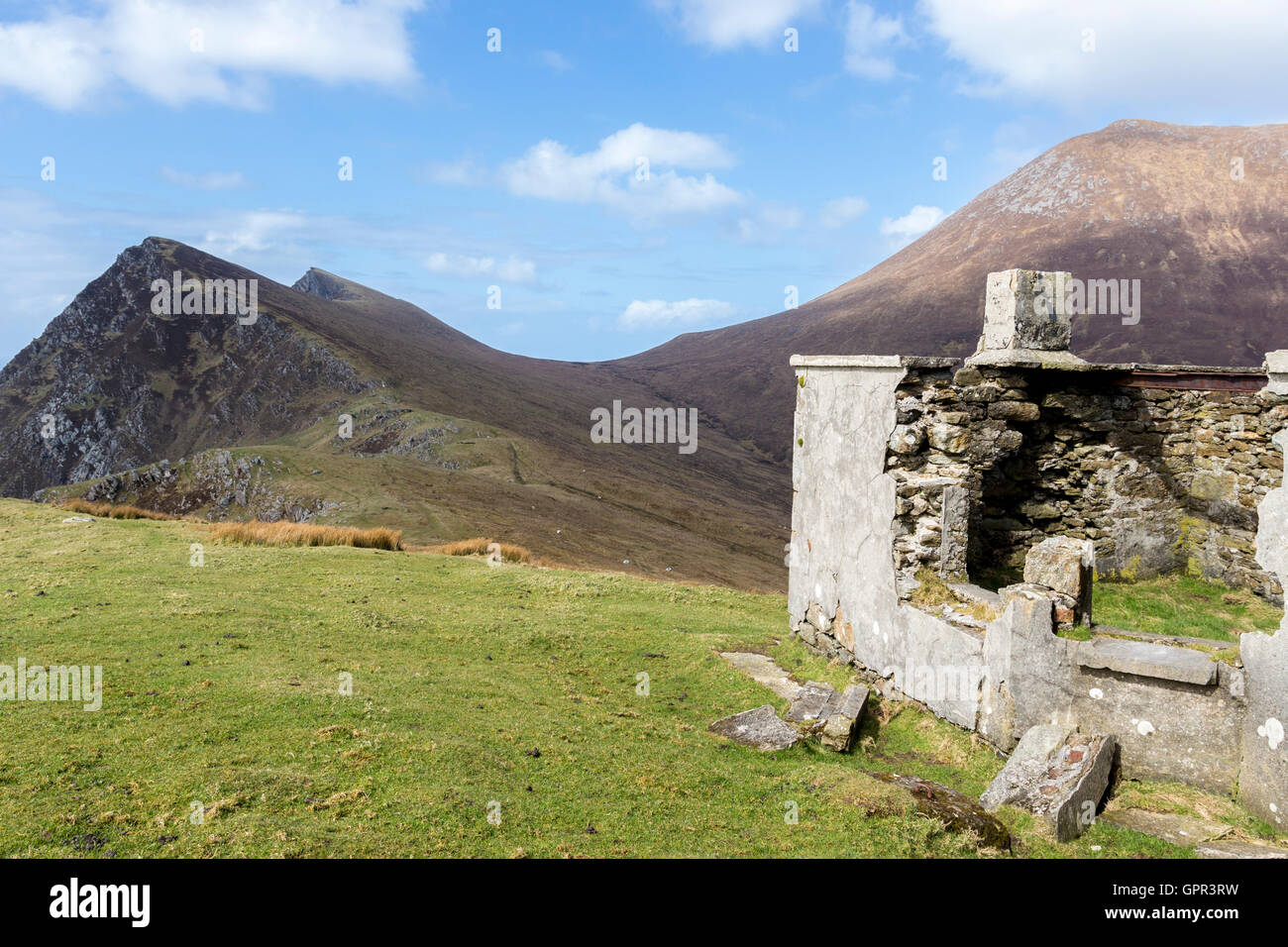 A derelict building on a remote hill with a mountain and cliffs in the ...