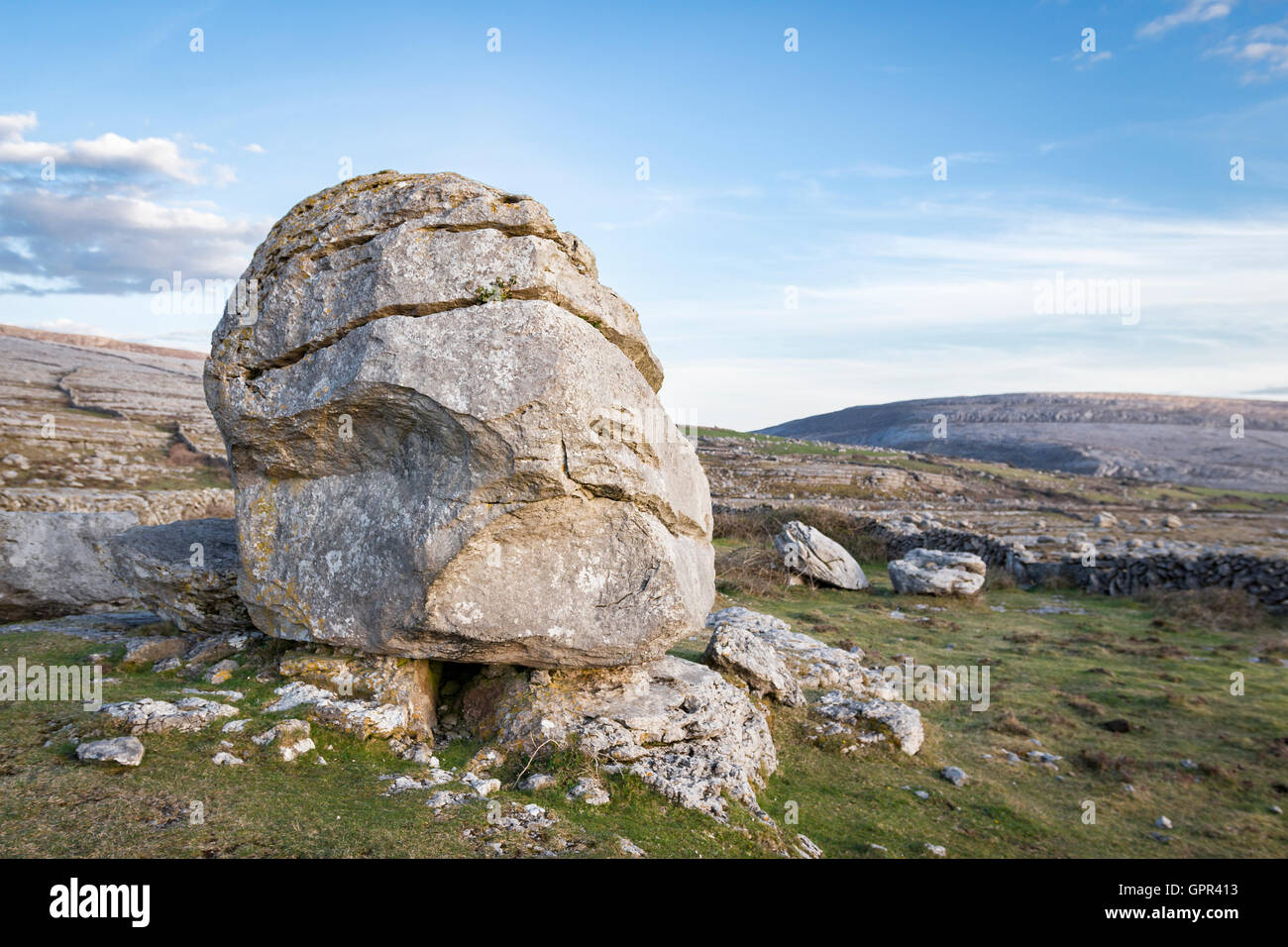A large boulder resting in a field bathed in warm evening light, with ...