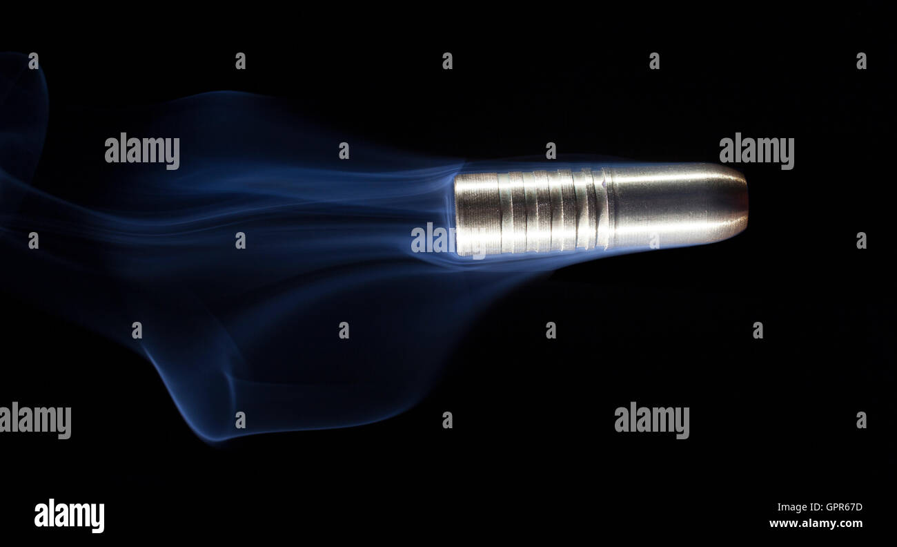 Big bronze colored bullet going past with smoke on a black background ...