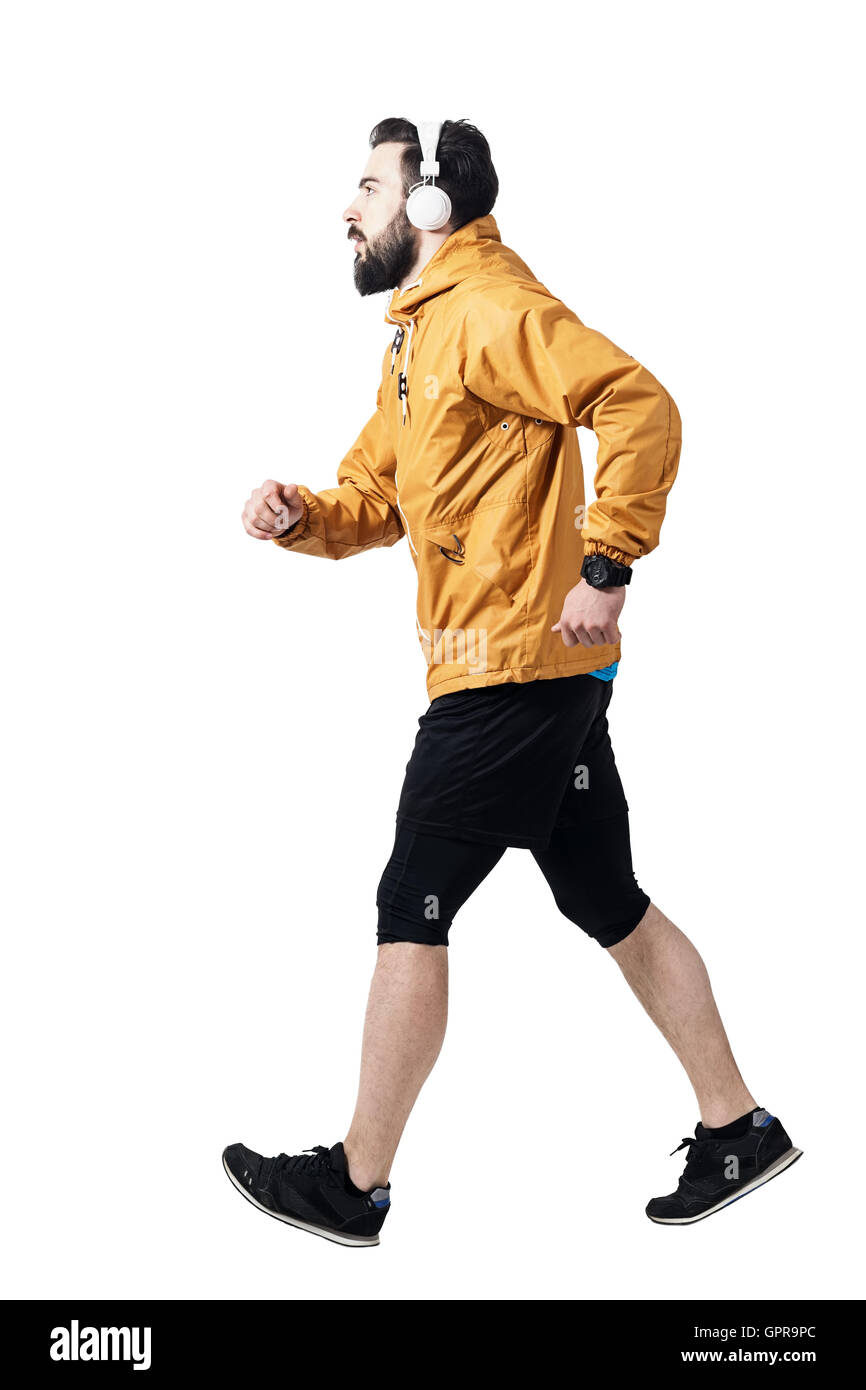 Side view of athlete jogging with headphones wearing jacket. Toned ...