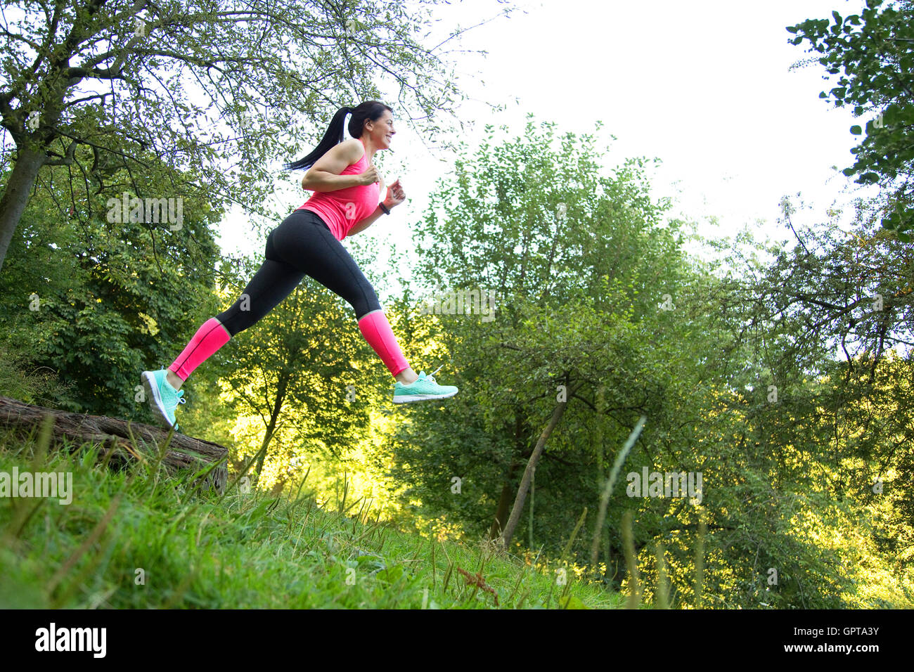 fitness girl out for a run jumping over a log Stock Photo - Alamy